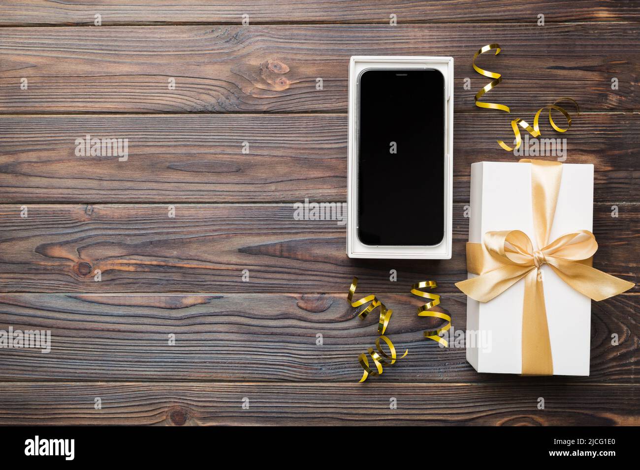 Opened gift box with gold ribbon and smartphone on color background ...