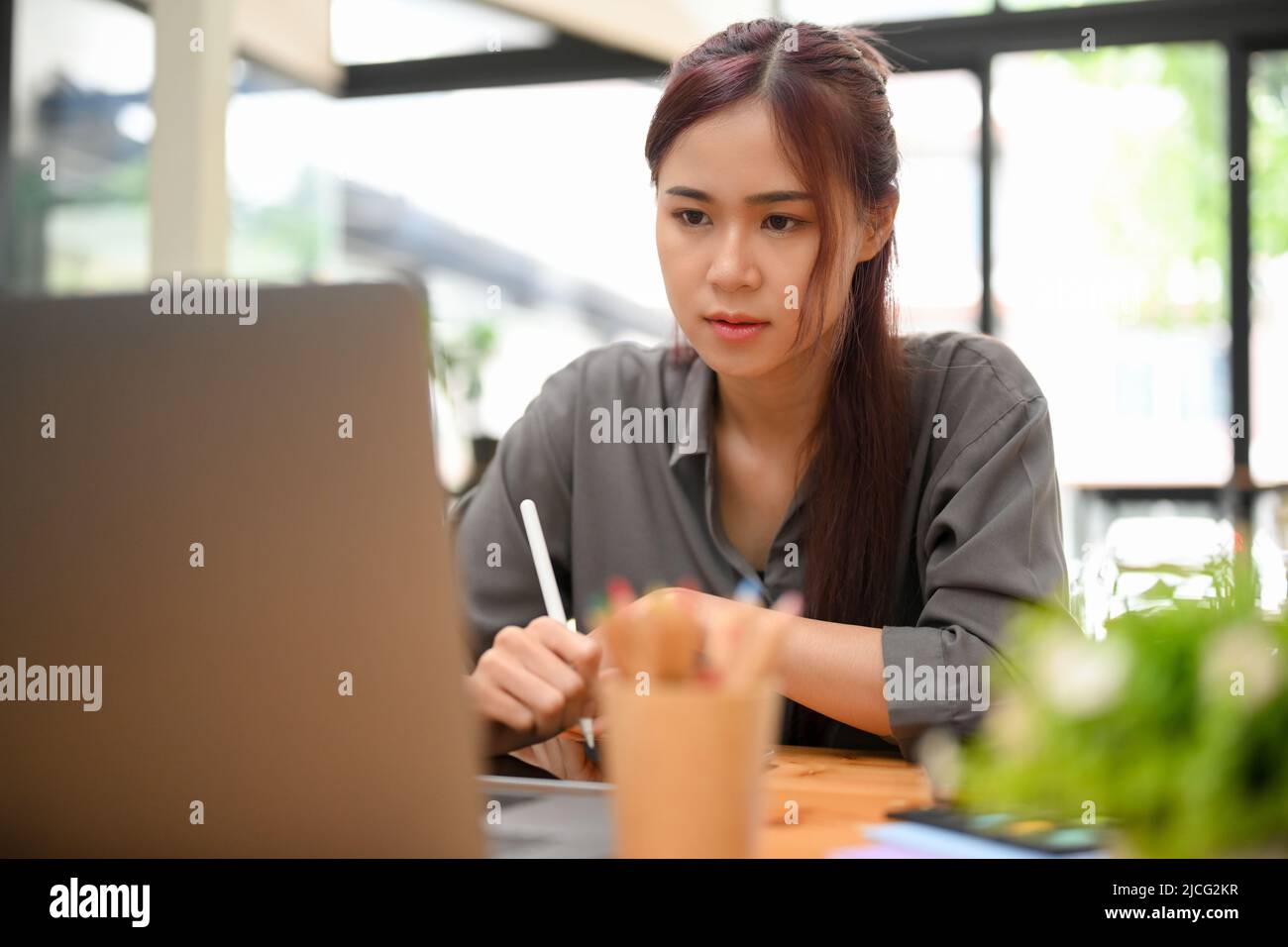 Beautiful young asian female graphic designer focused on her work, sits ...
