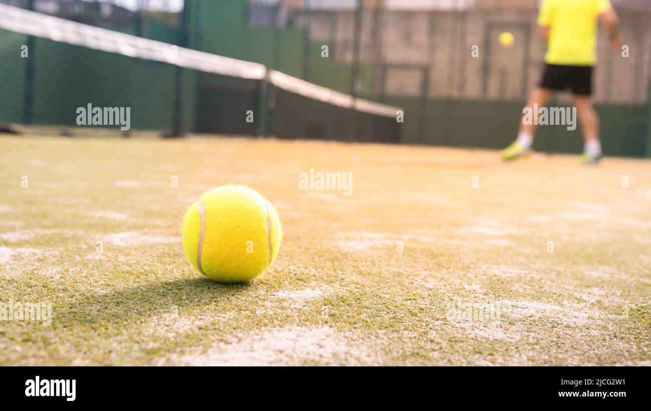 Yellow ball on floor behind paddle net in green court outdoors. Padel ...