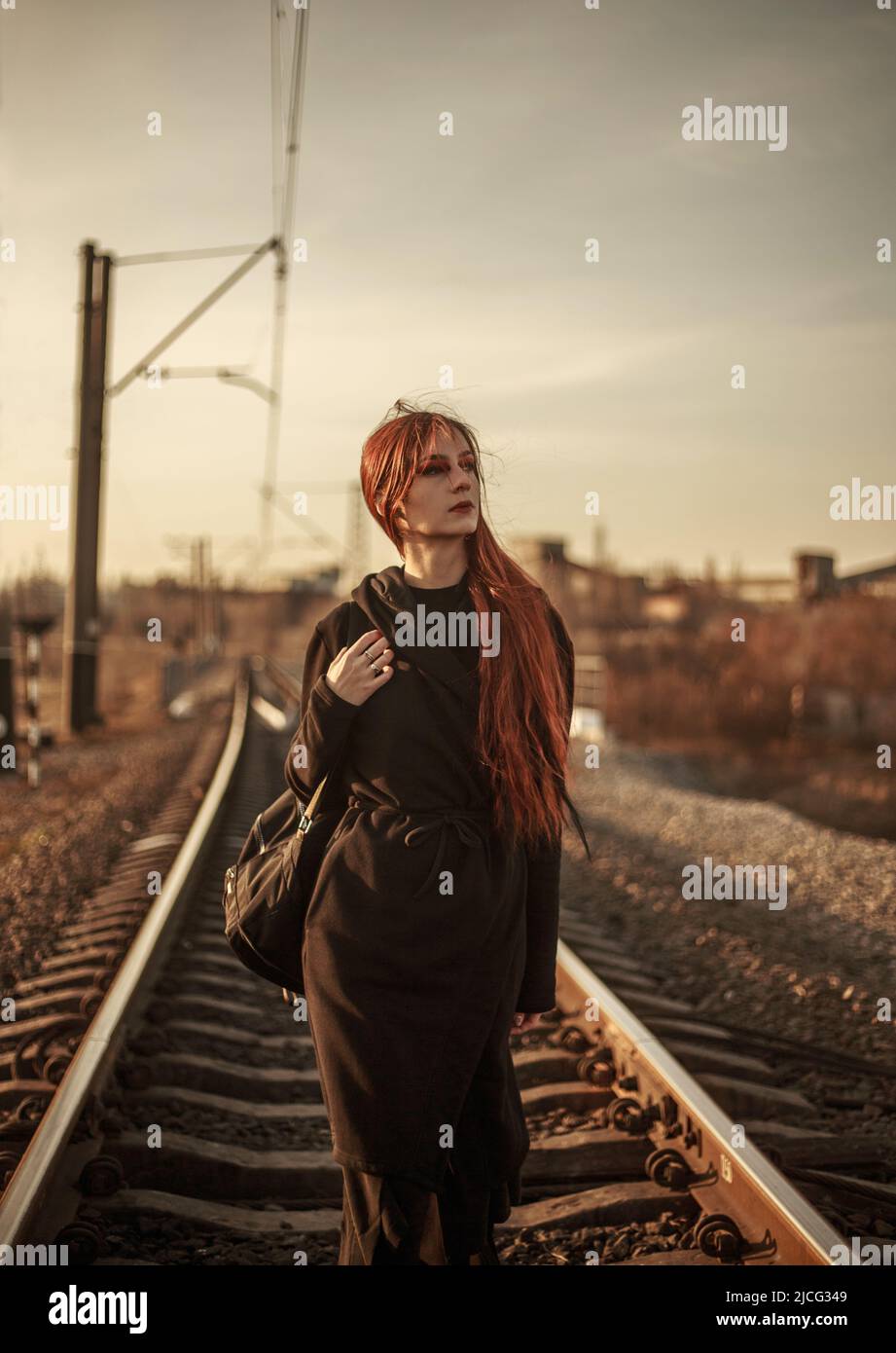 Young lonely woman walking along a railway track, on the background of ...