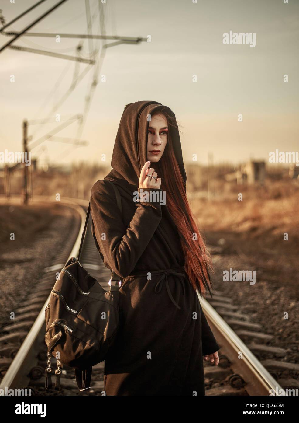 Young lonely woman walking along a railway track, on the background of ...