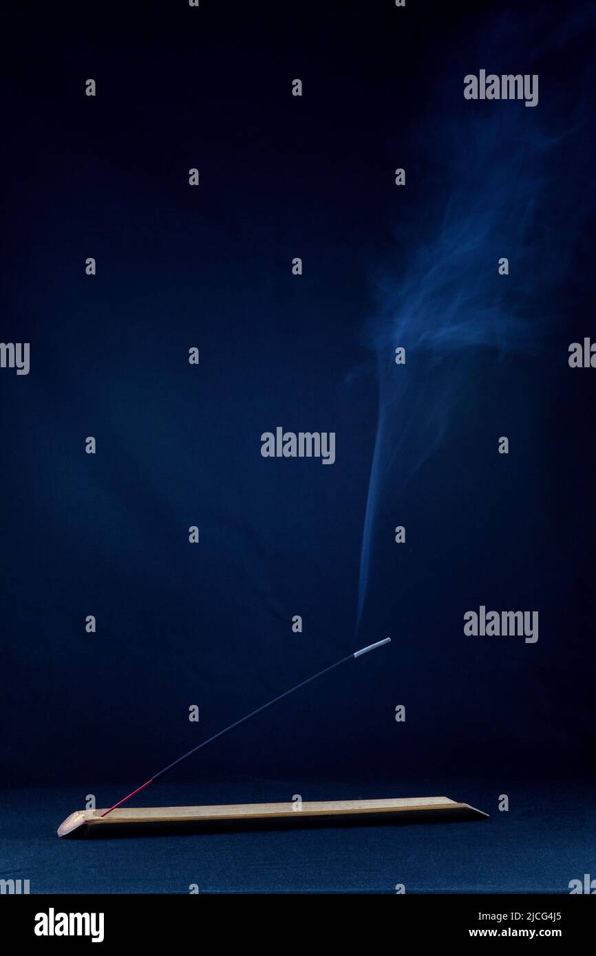 Burning stick of incense in a bamboo holder on a blue cloth background ...