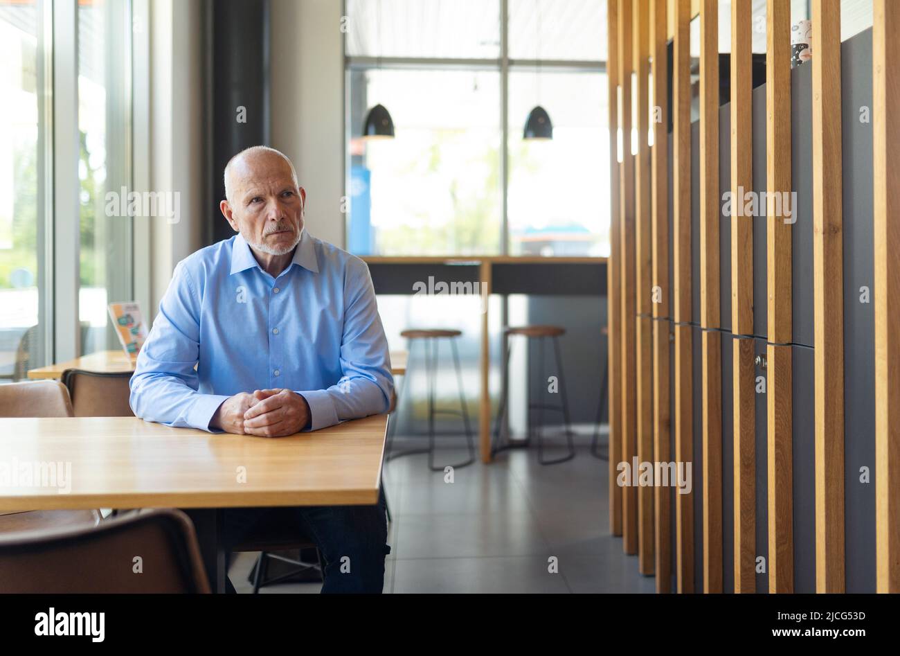 Sad senior man sitting at empty table with blurred cafe interior in ...