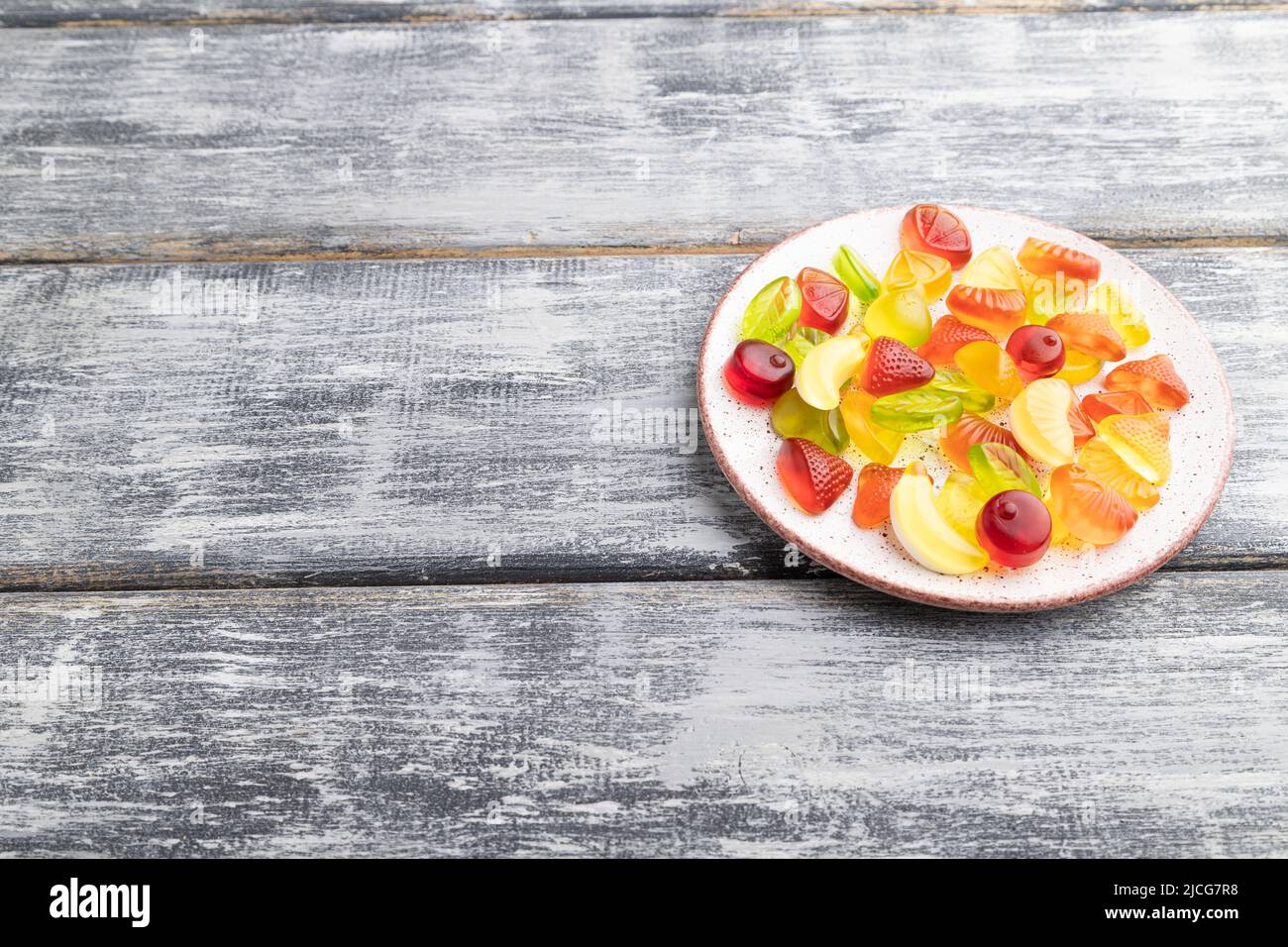 Various fruit jelly candies on plate on gray wooden background. side ...