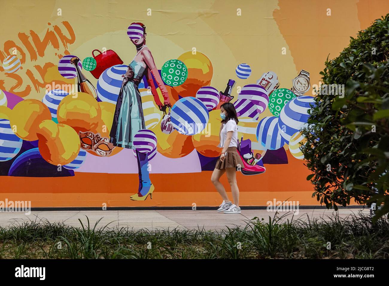 A woman wearing a face mask walks past a giant advertising poster ...