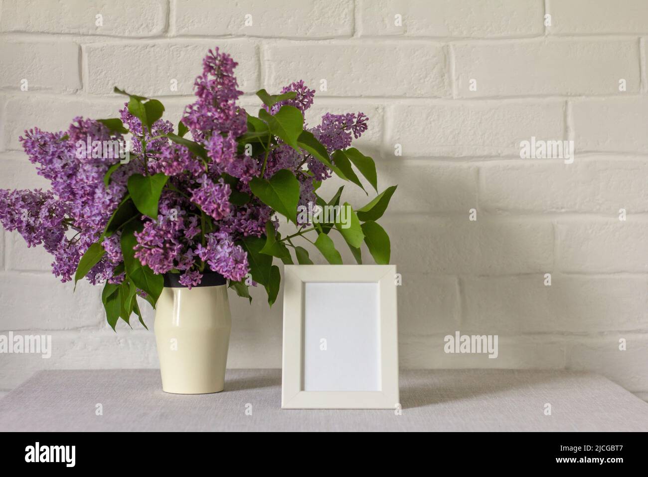 Mockup of a white photo frame on the table and a bouquet of lilacs in a ...