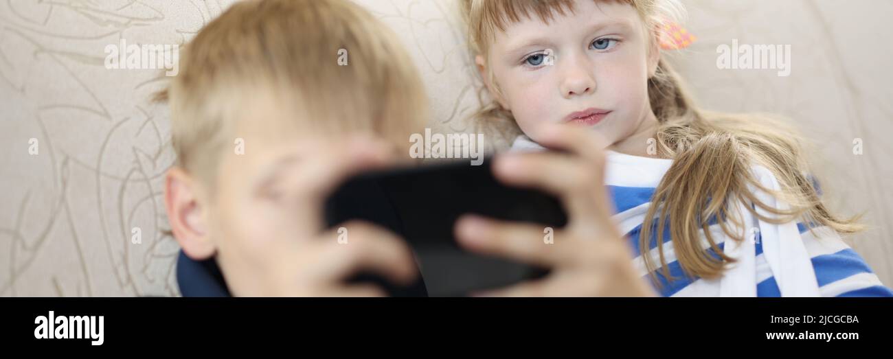 Brother and sister at home on sofa watching on smartphone screen Stock ...