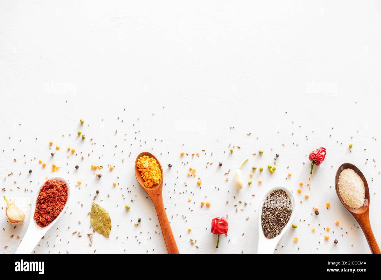 spices and seasonings in spoons and scattered on a white background ...