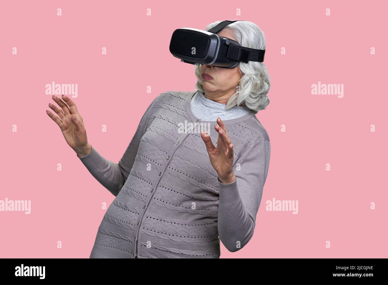 Stunned senior woman with virtual reality headset on pink background ...