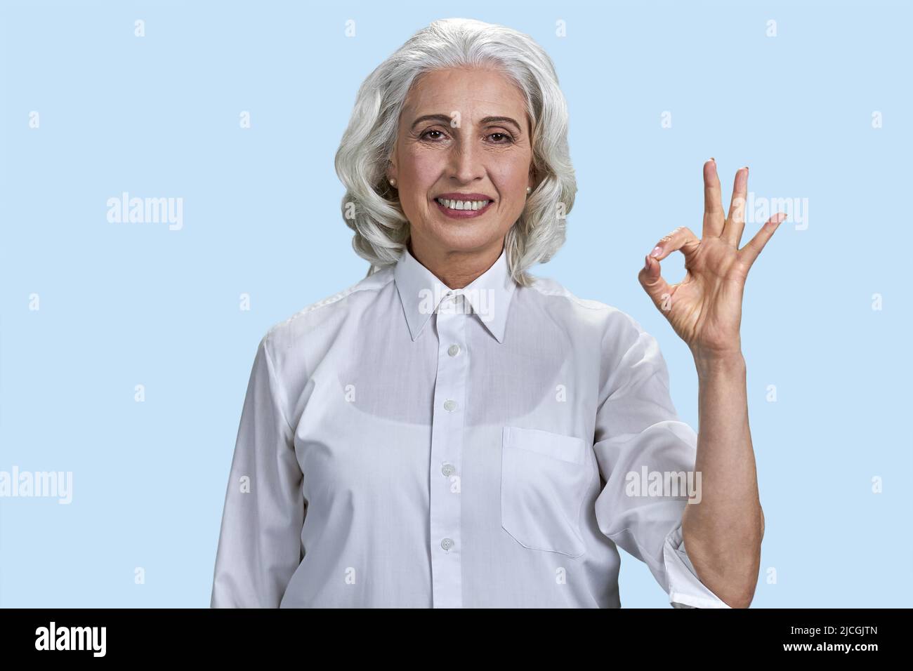 Portrait of happy grandmother gesturing okay on blue background. Happy ...
