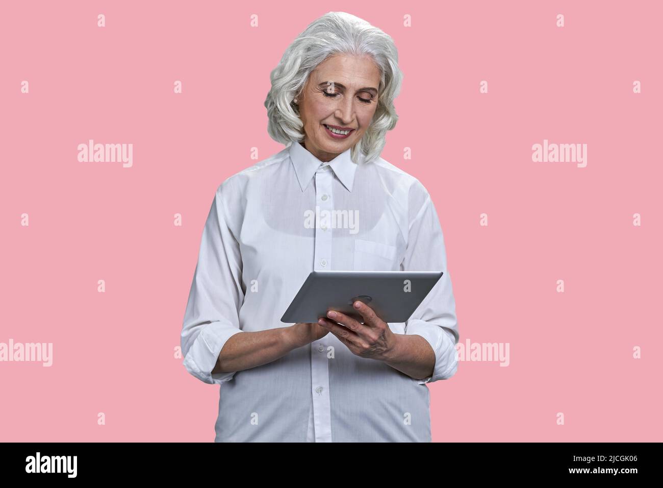Pretty senior woman holding digital tablet on pink background. Smiling ...