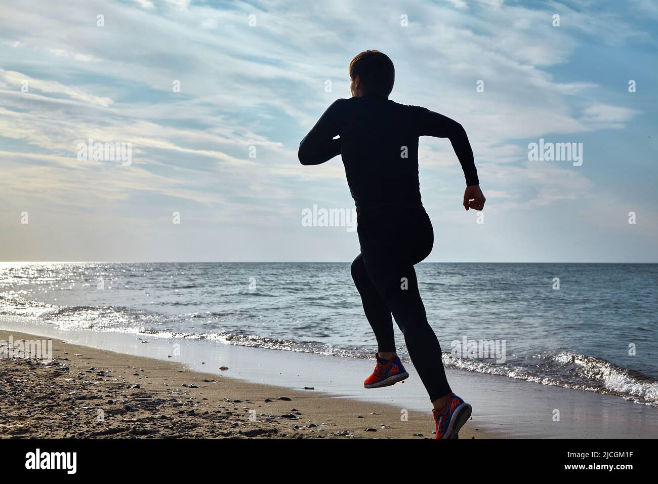 A young man in a sports uniform runs along the seashore. Aerobic ...
