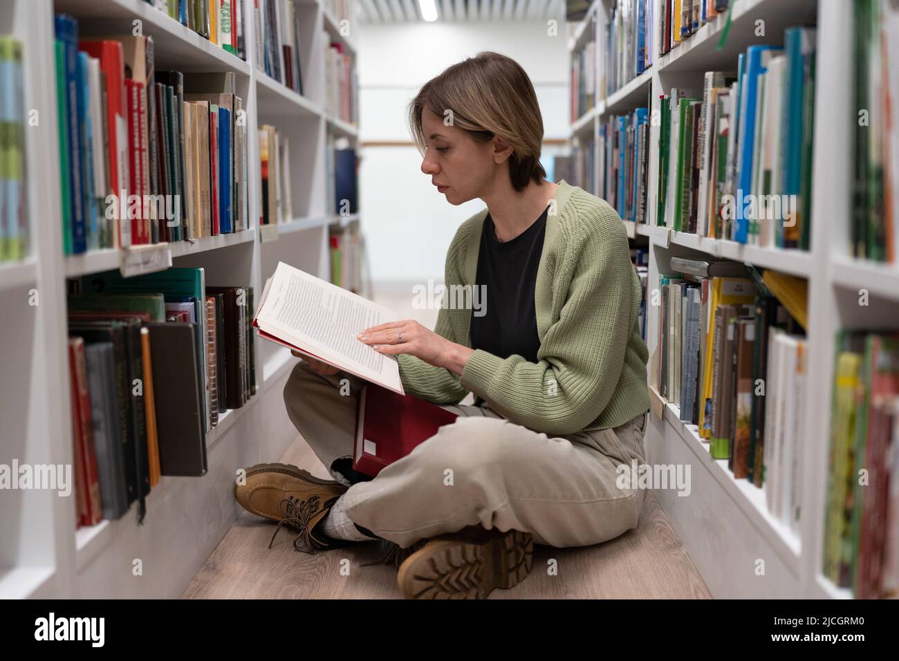 Focused woman teacher in casual clothes sits with textbook, prepares ...