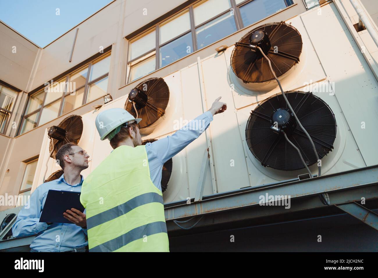 Service engineers in uniform inspecting industrial refrigeration system ...