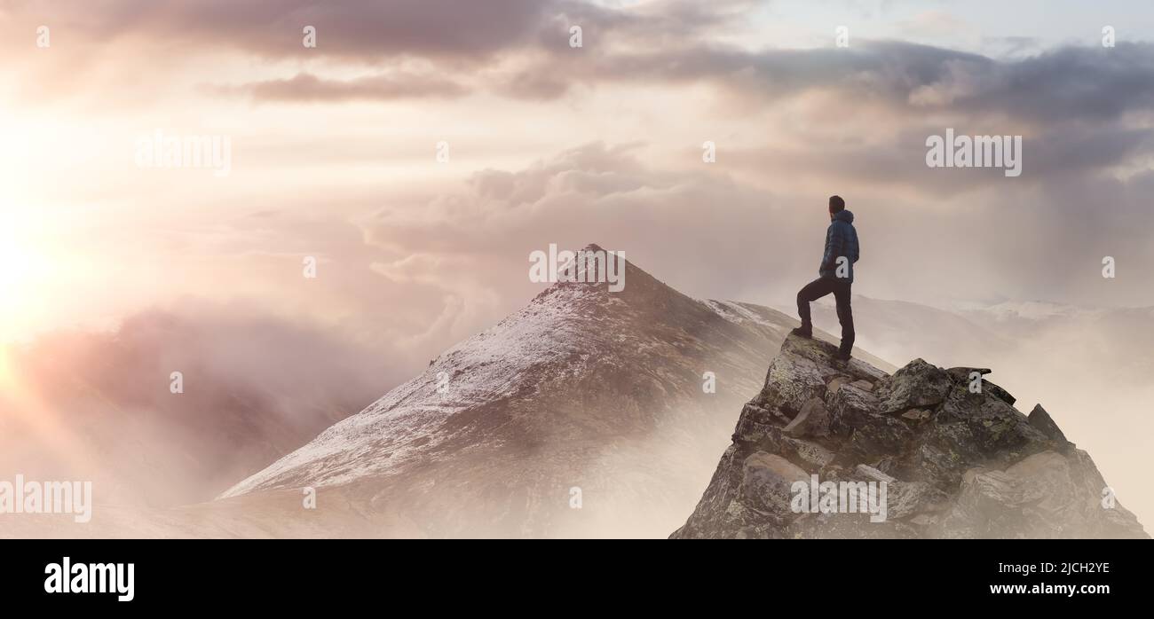 Adventurous Man Hiker standing on top of icy peak with rocky mountains ...