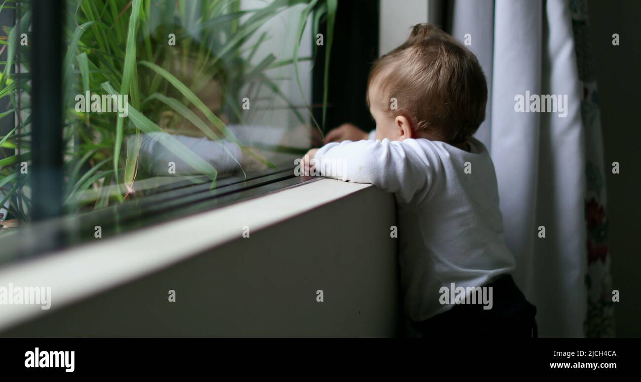 Cute baby boy standing by window feeling bored Stock Photo - Alamy
