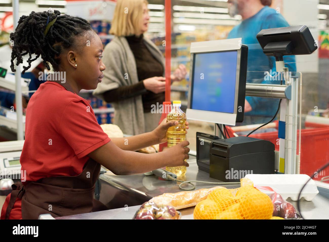 Black saleswoman checking price of sunflower oil while holding plastic ...