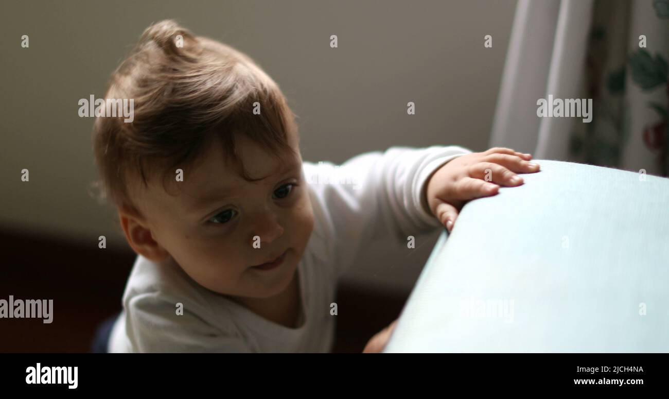 Cute baby learning to stand by supporting on furniture. Infant child ...