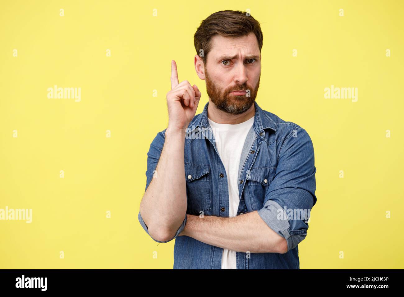 Focused man raised finger up as sign he has new idea on yellow studio ...