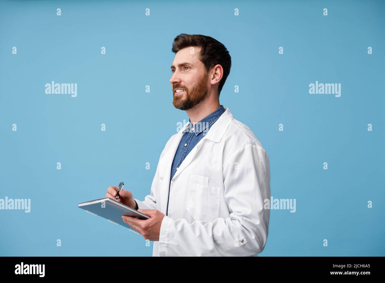 Doctor making medical notes in clipboard standing over blue studio ...
