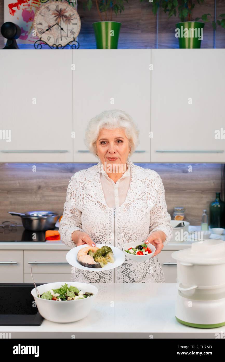 Grandmother in the kitchen prepares a healthy meal of steamed fish with ...