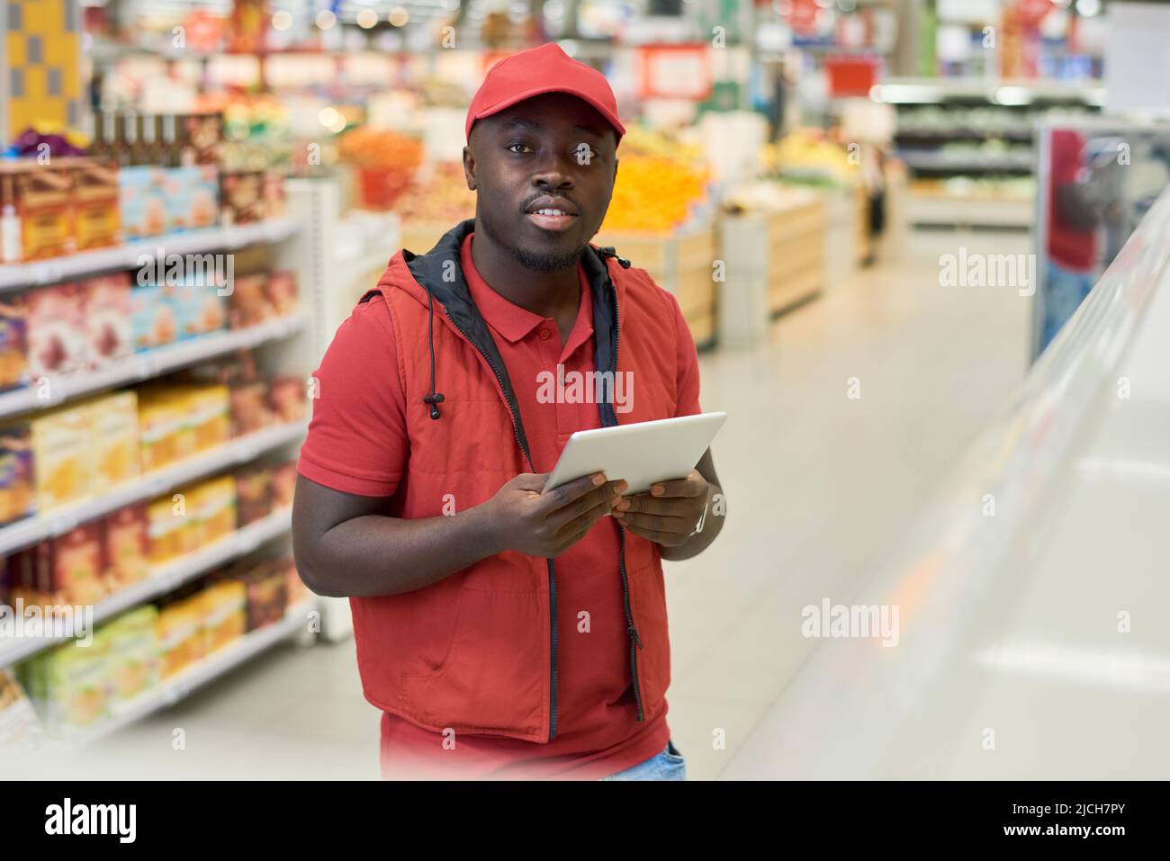 African American guy in red uniform and cap using digital tablet in ...