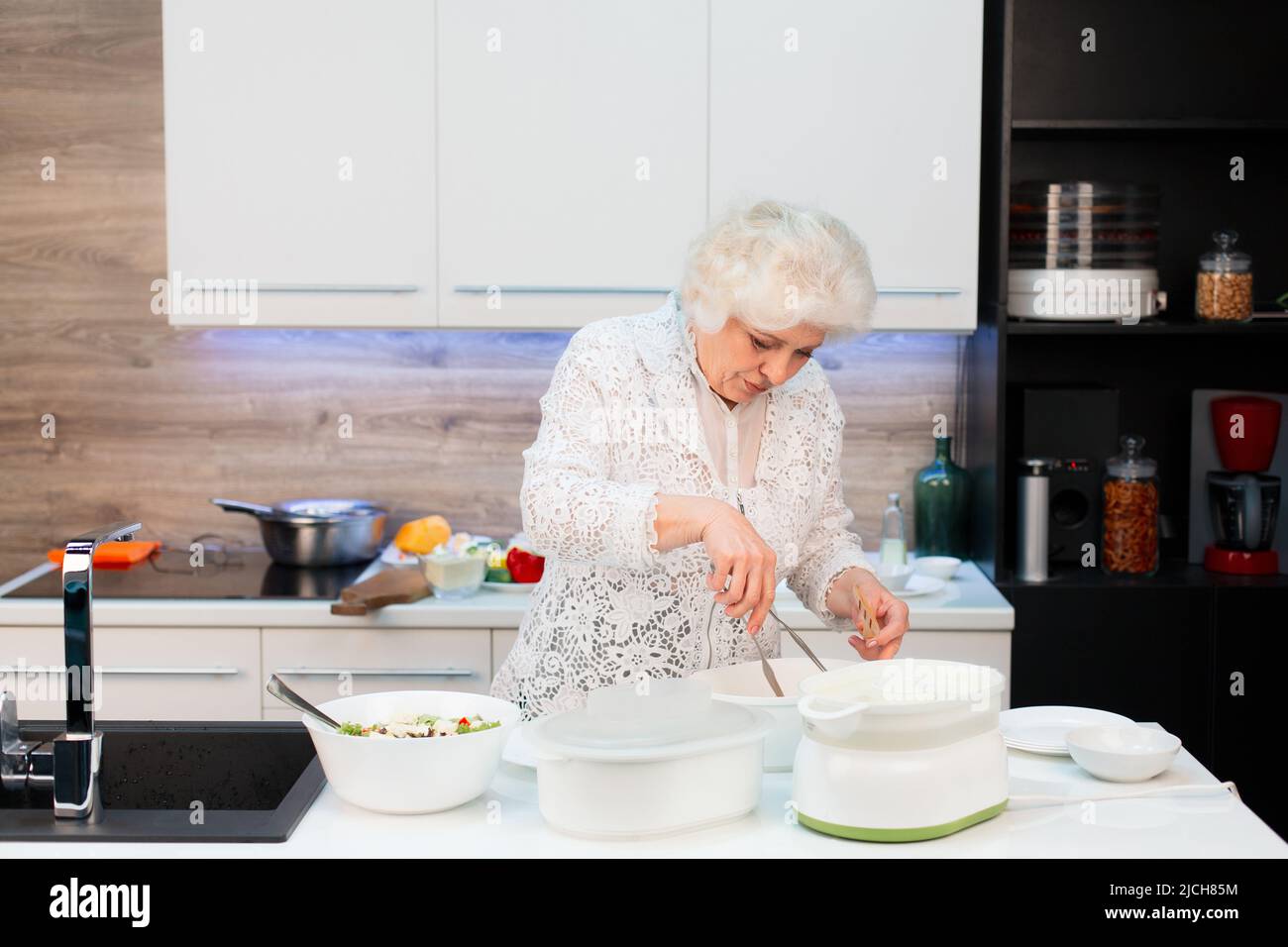 The older woman in the kitchen cooks healthy food in a double boiler ...