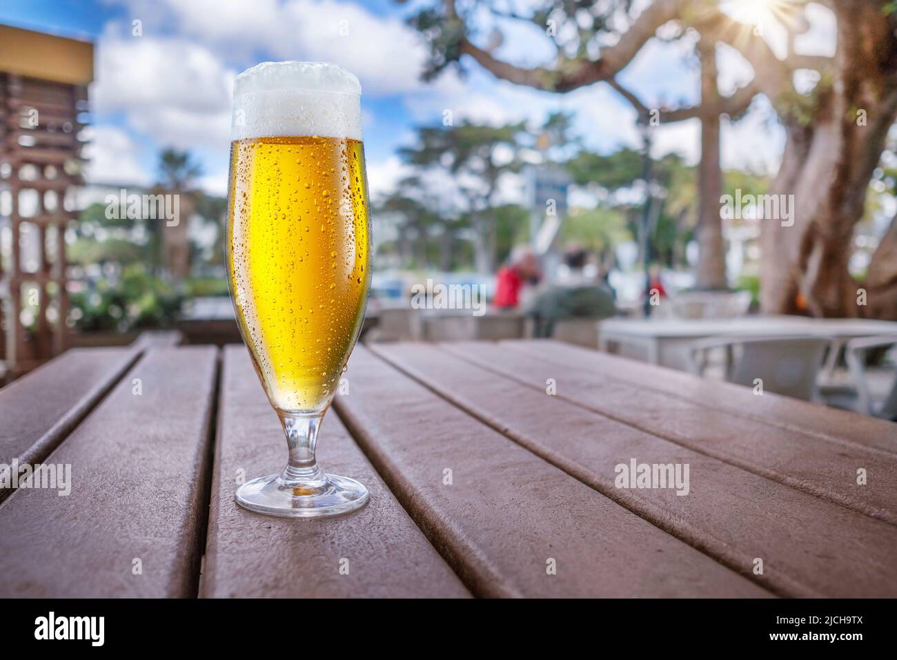 Cooled glass of beer on the wooden table. Blurred summer street cafe ...