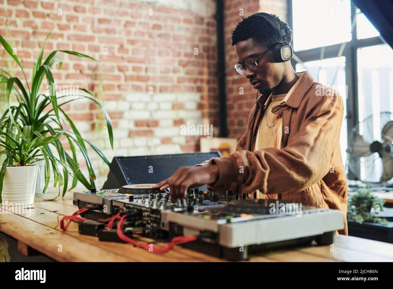 Serious young black man with headphones on his head mixing sounds while ...