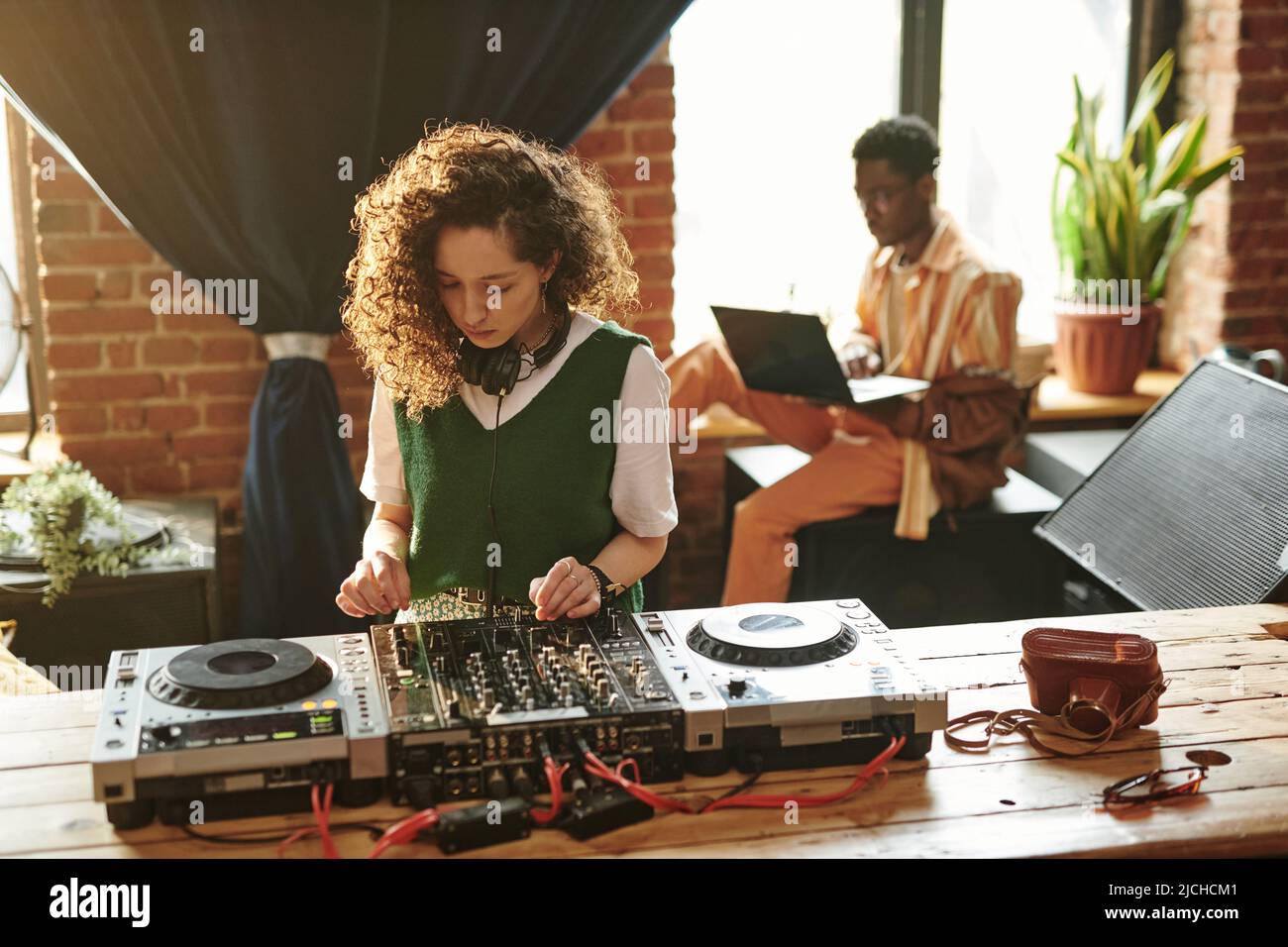 Young woman in casualwear standing by wooden table and using dj ...