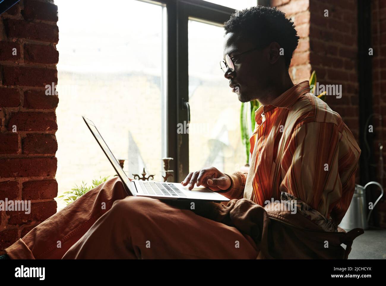 Side view of young black man looking at laptop screen while sitting ...