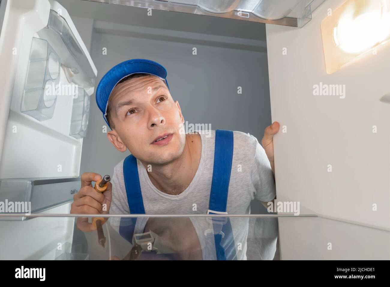 Male technician in overalls repairs a broken refrigerator with a ...