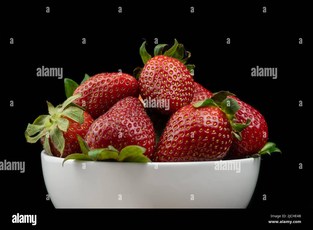 Ripe red strawberries with green tails in a white plate on a black ...