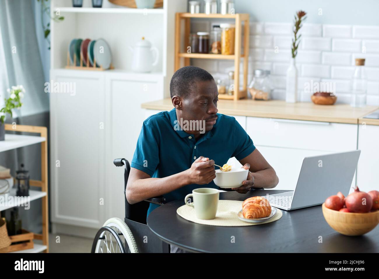 Portrait of black adult man with disability eating breakfast at table ...