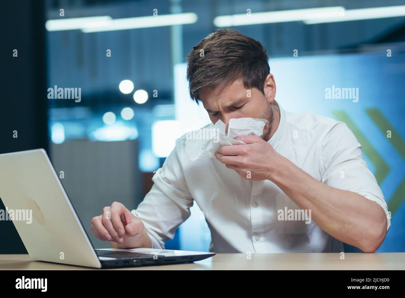 A businessman at work is sick, coughs and has a runny nose, sits at a ...