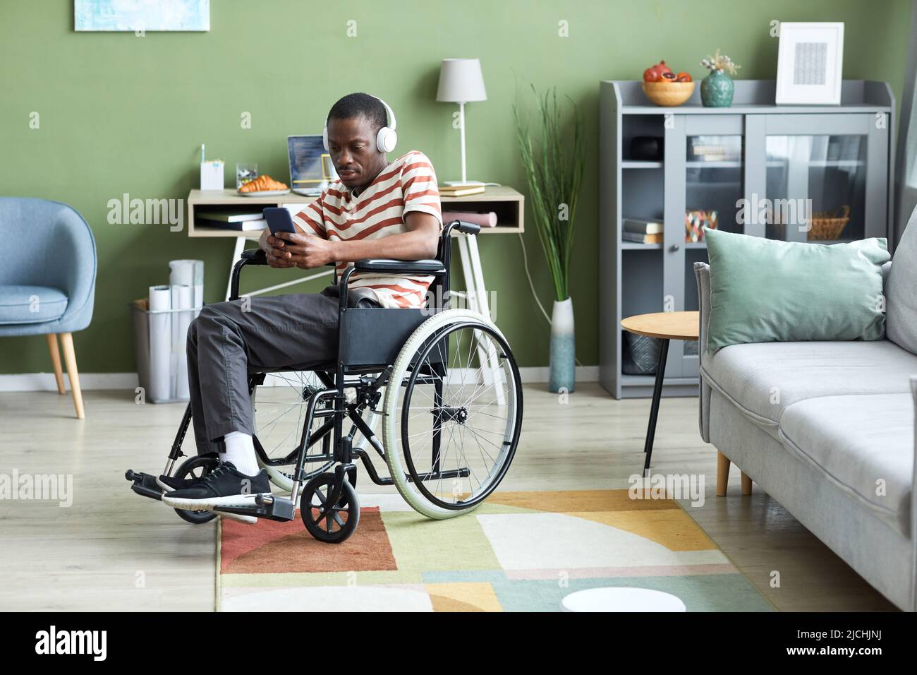 Full length portrait of black man with disability using smartphone and ...
