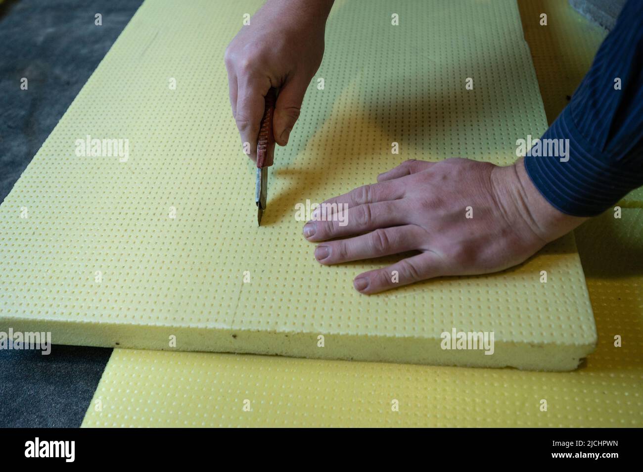 The master cuts expanded polystyrene on a floor, installation and ...