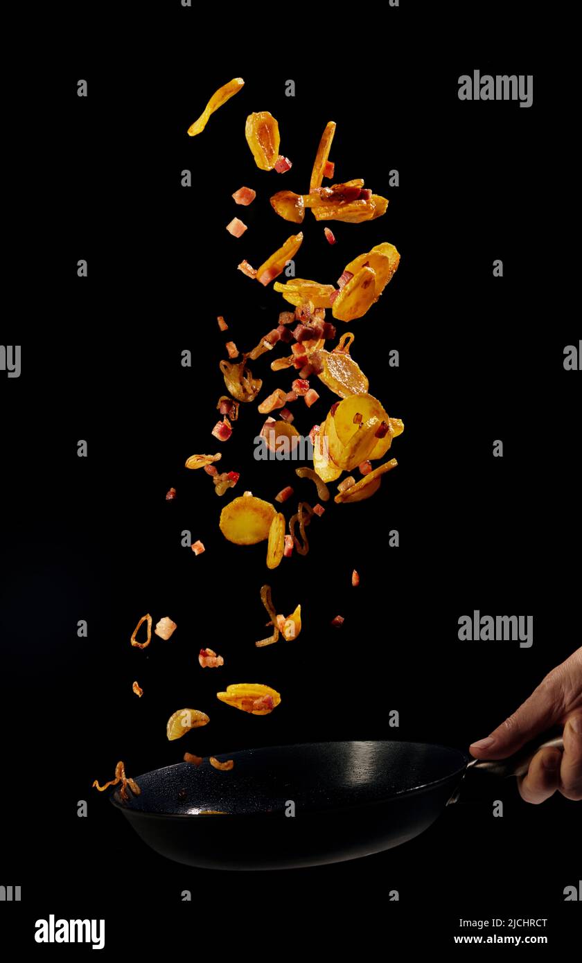 Crop anonymous chef tossing fried potatoes with bacon in metal frying ...