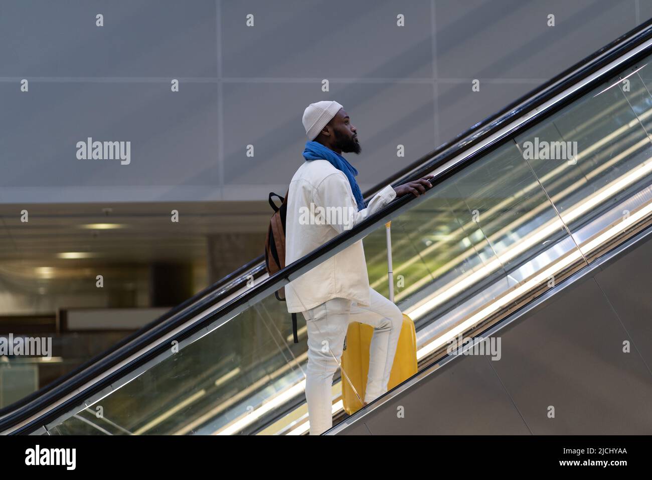 African American passenger man with suitcase stands on escalator, holds ...