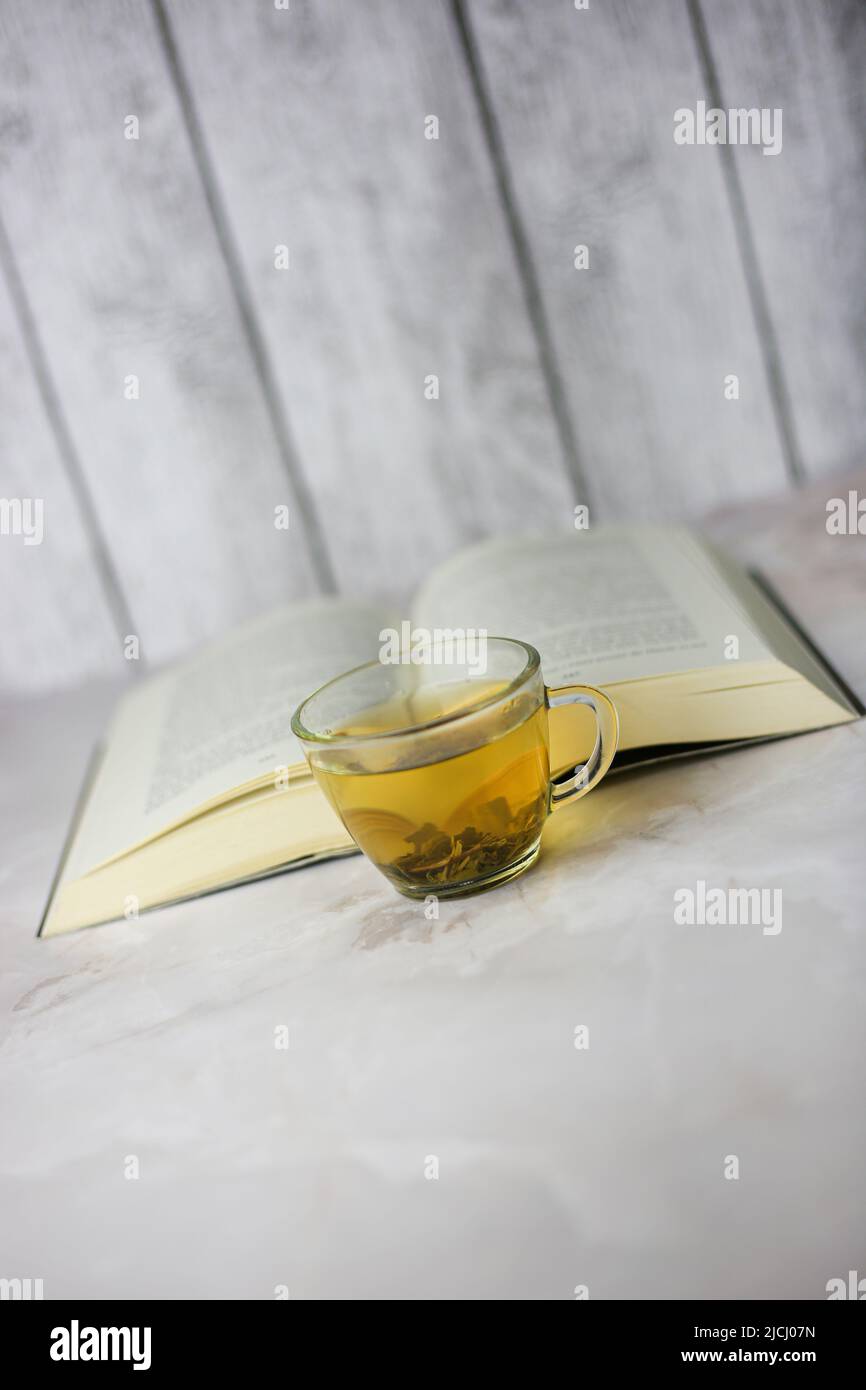 Brewed herbal green tea in a transparent cup in front of an open book ...