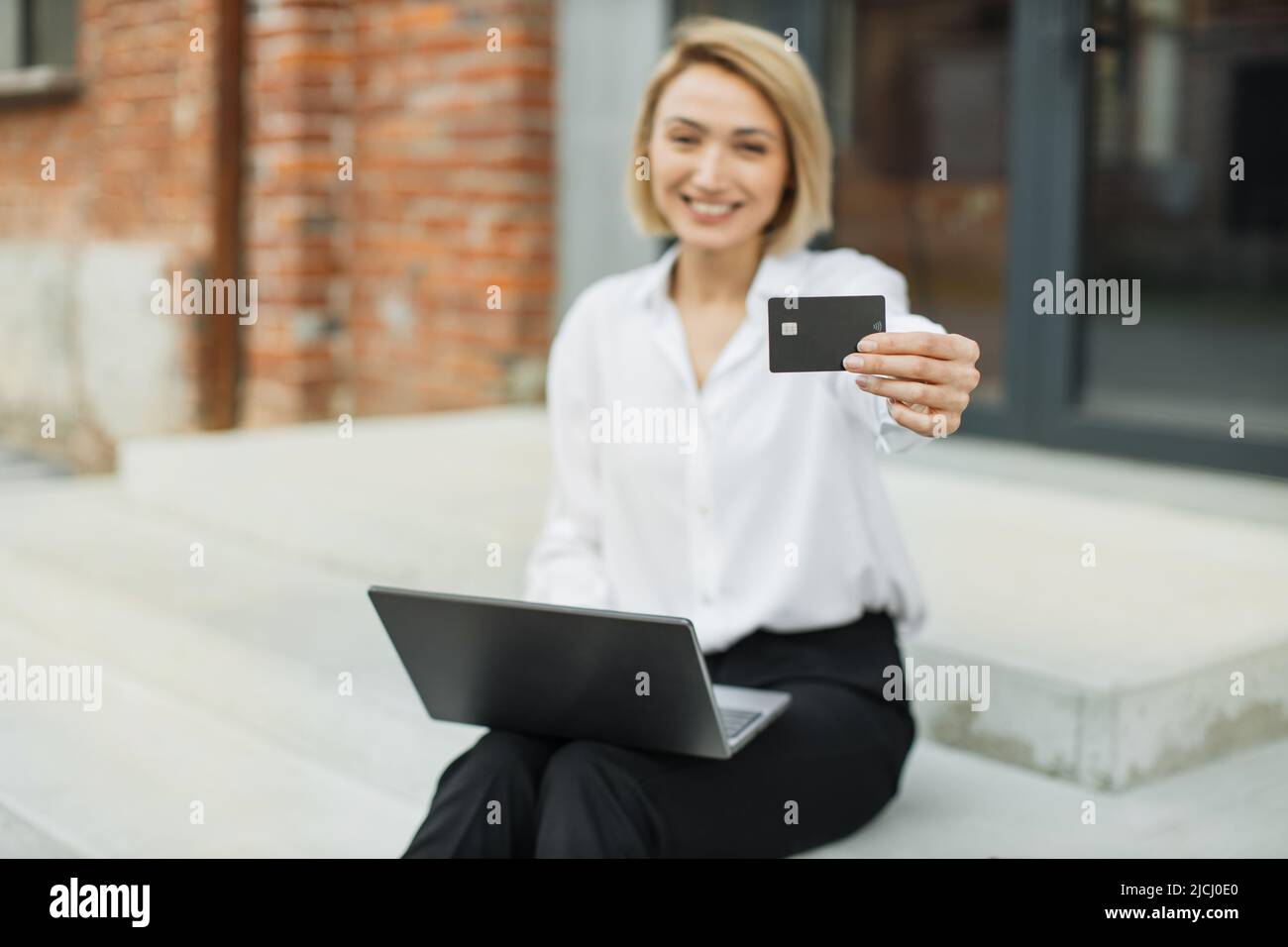 Focus on bank credit card. Business payment of bills concept. Smiling young woman, using ...