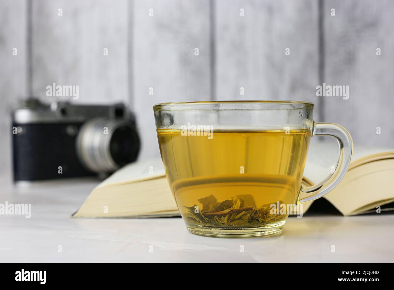 Brewed herbal green tea in a transparent cup next to an open book and a ...