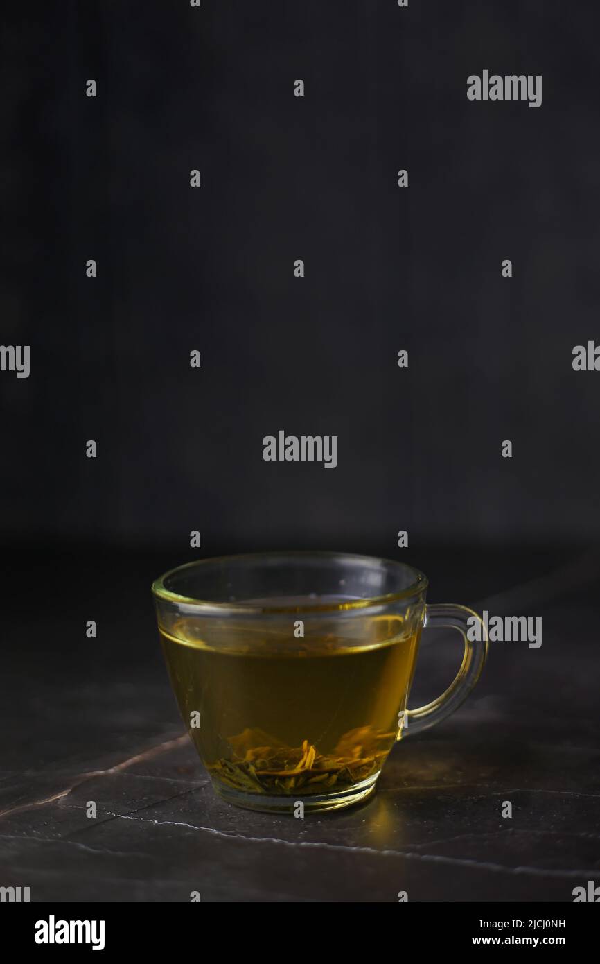 Illuminated brewed herbal green tea in a transparent cup on a dark ...