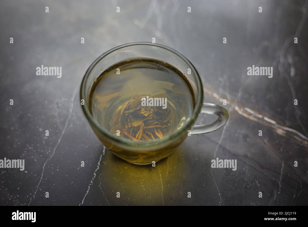 Illuminated brewed herbal green tea in a transparent cup on a dark ...