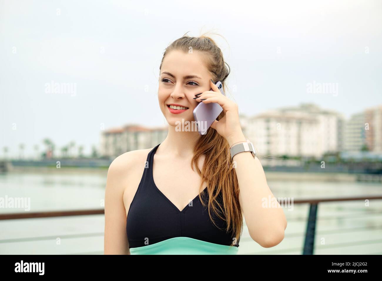 Happy brunette woman wearing black sports bra standing on city park ...