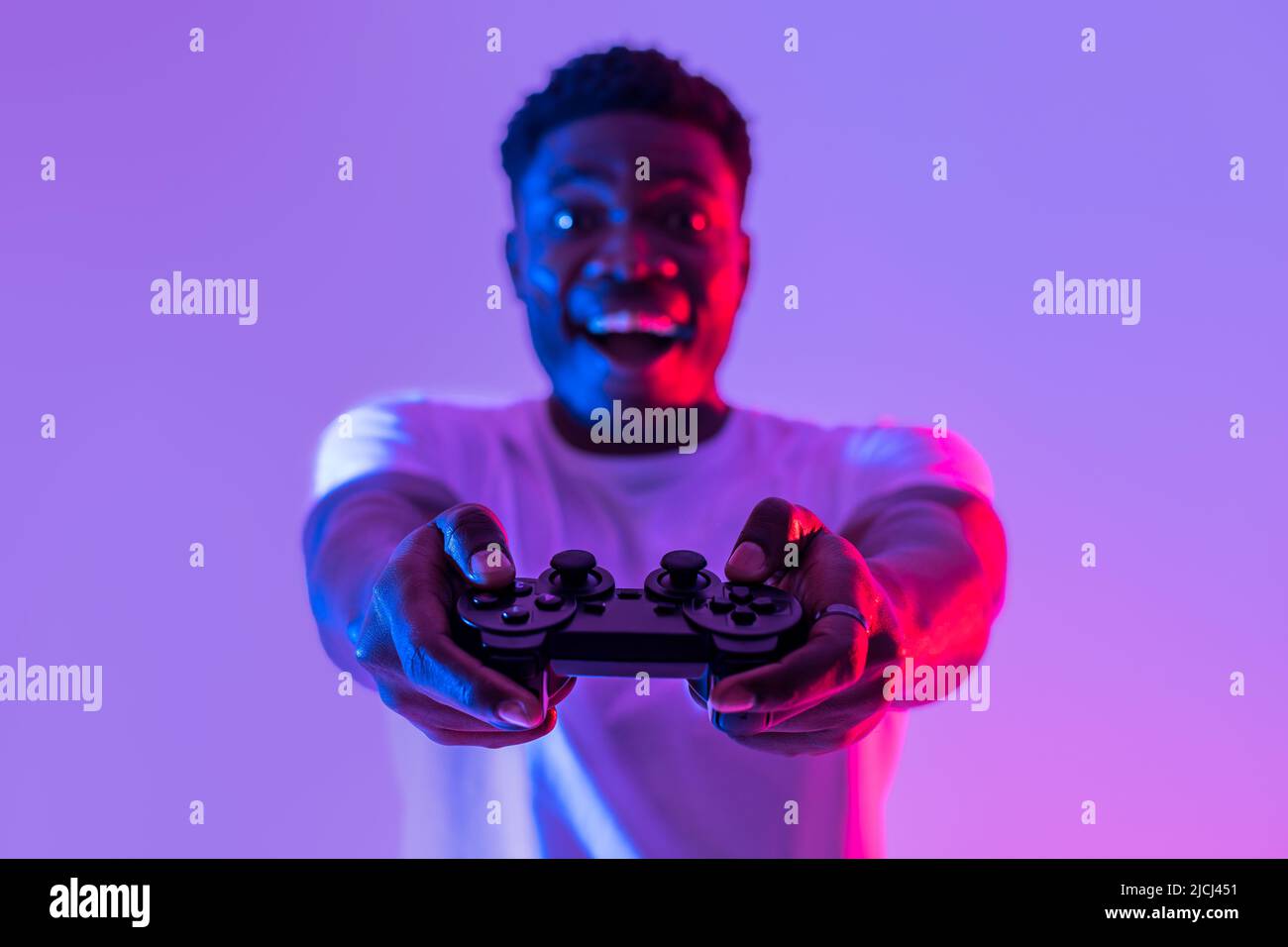Happy young black guy with joystick playing video game in neon light ...