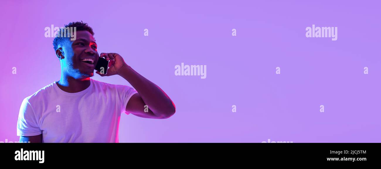 Happy young black man talking on smartphone in neon light, banner ...
