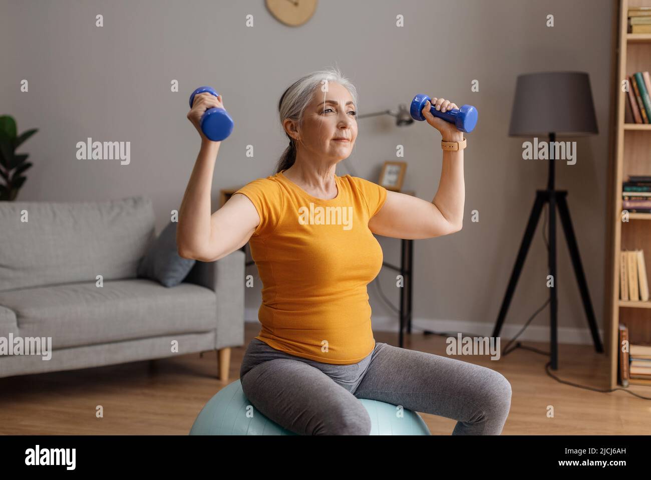 Stay home, do sports. Fit senior woman doing exercises on fitness ball ...