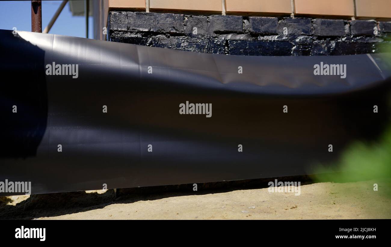 Waterproofing the foundation of the house with black mortar. Brick wall ...