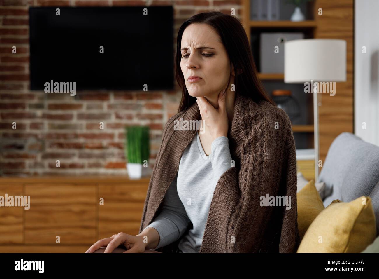 Portrait of ill young woman at home having cough and sore throat. First symptoms of cold and flu ...